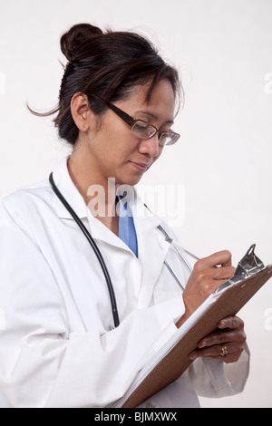 Asian female doctor writing medical notes in bright modern clinic ...