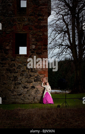 A woman with blonde hair leans against a stone pillar, gazing off into ...