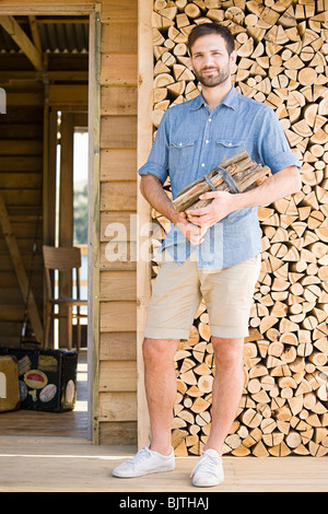 man holding a log of wood and standing in front of mud wall, Burundi ...