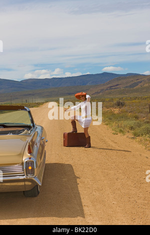 Woman hitchhiker standing on the side of the road in autumn forest ...