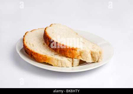Two slices of white bread are side by side on a white plate; the first ...