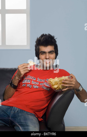 Young hispanic man holding potato chips celebrating victory with happy ...