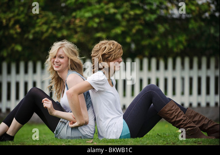 Two girls sitting back to back Stock Photo - Alamy