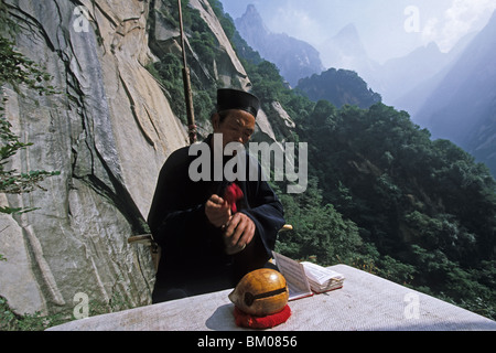 Taoist hermit monk prays in front of his hut, cliff, Hua Shan, Shaanxi ...