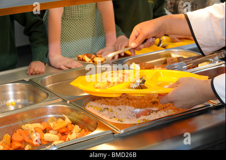A dinner lady serves up school dinners in a canteen over a hot plate ...