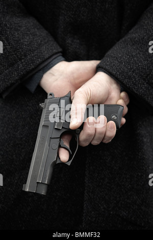 Man holding a loaded gun behind his back Stock Photo - Alamy