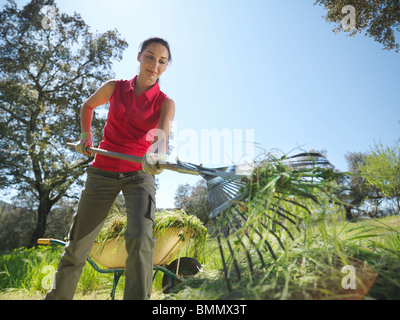 Female farm worker raking hay into rows with tractor with baler at work ...