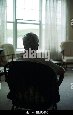 Old woman from behind as she looks out window. Old man reads in other ...