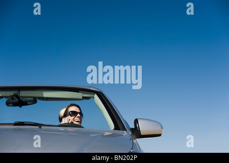 Woman driving and smiling while talking on a mobile phone in a car ...
