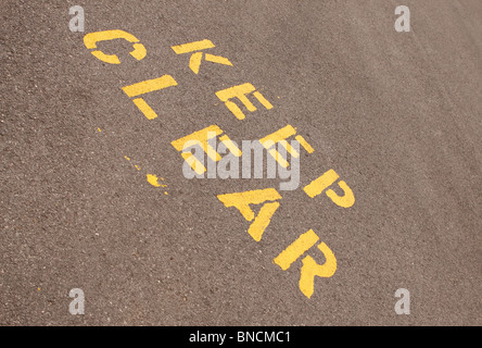 Yellow Keep Clear road sign, written on road at entrance to park in ...