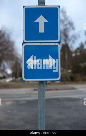 A blue traffic sign with directional arrows is mounted on a wall in a ...