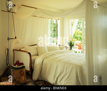 White voile drapes above bed with white linen in cottage bedroom with ...