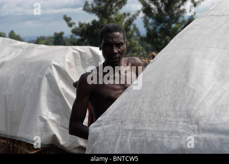 A displaced Congolese man stands amid straw huts covered with plastic ...