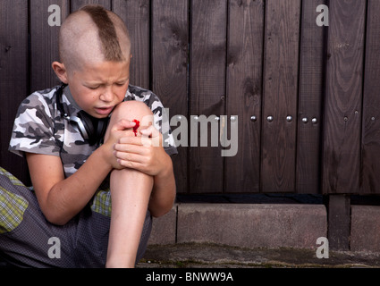 Young injured boy with bleeding knee sitting down outside Stock Photo ...