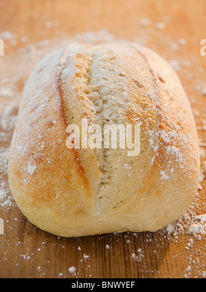 A vertical shot of a freshly-baked loaf of bread sitting atop a wooden ...