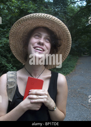 Smiling young woman in a straw hat holds a camera on a rocky beach. She ...