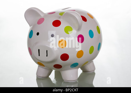 White polka dot piggy bank with male hand depositing money Stock Photo ...