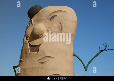A cement statue of a giant potato man stands beside the the road on the ...