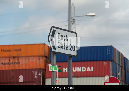 A road sign showing the words 'Dock Gate 20' with shipping containers ...