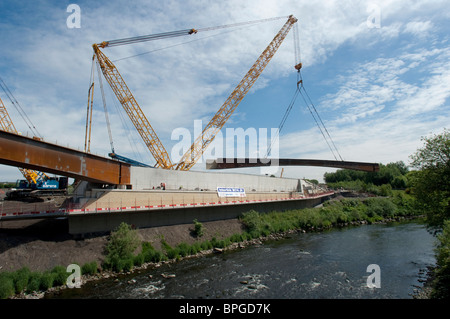 Construction workers move a steel bridge by crane into position over ...