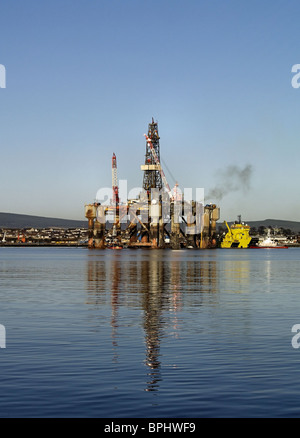 An oil drilling rig is reflected in the water of the reserve pit as a ...