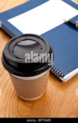 a Cup of drink and a paper notebook with a black pen on a blue wooden ...