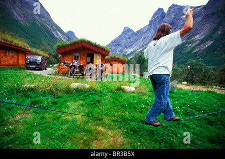 Man slacklining in front of grass covered cabin and friends in high ...