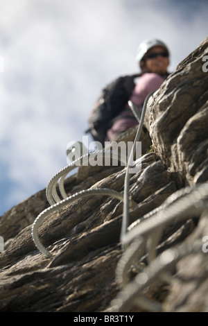A young woman climbing a ladder embedded in the rock while engaging in ...