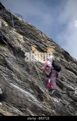 A young woman climbing a ladder embedded in the rock while engaging in ...