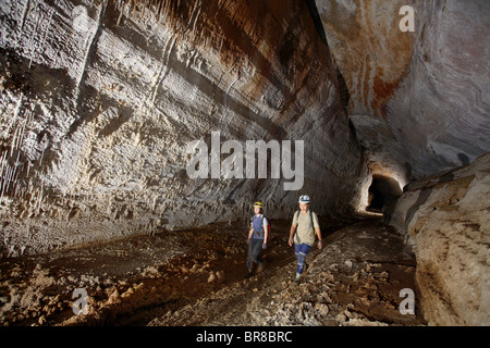 Two female cave explorers walk through a tunnel in a cave deep in the ...