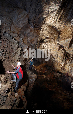Two cave explorers traverse a section of cave on a ledge above a deep ...