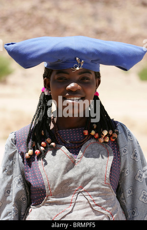 Herero woman in costume, with headdress and vessel in hand on a sand ...