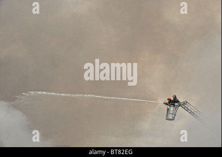 Firemen on an extension ladder fighting a massive factory fire amidst ...