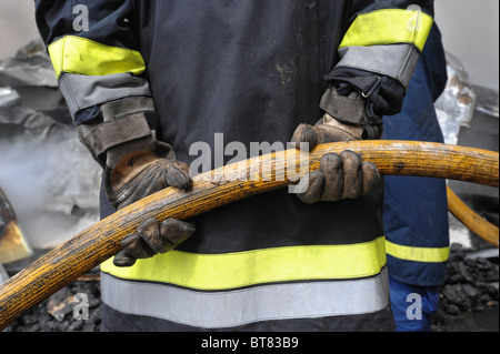 A fire fighter is holding the fire hose over his shoulder ready to ...