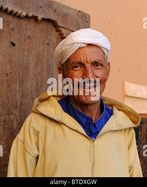 Smiling Moroccan man in djellaba and cap against an old door in el Bali ...
