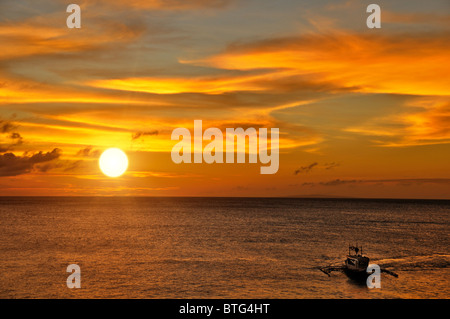 Sailboat sailing towards the horizon at a warm orange cloudy sunset ...
