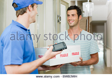 Young delivery man delivering package to businessman against gray Stock ...
