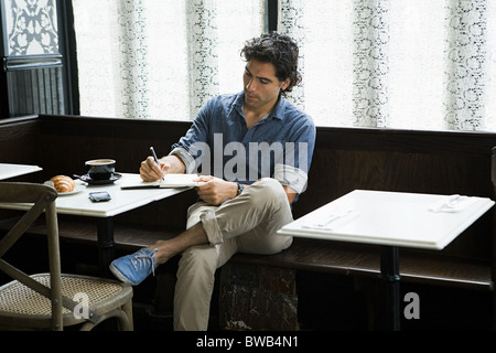 Young hispanic man writing book sitting on the table sticking tongue ...