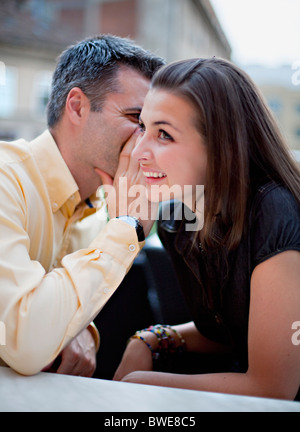 Side view of girlfriend whispering secret into surprised boyfriend's ...