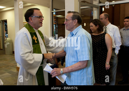 Anglo male pastor shakes hand of elderly Anglo female as congregation ...