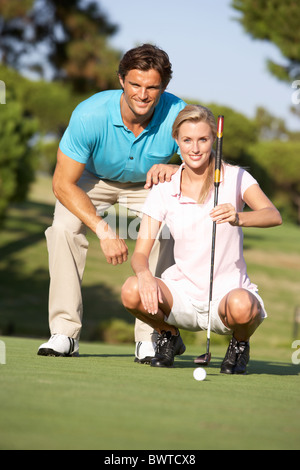 Female golfer lining up a putt kneeling on the green looking at the hole to check the grass and ...