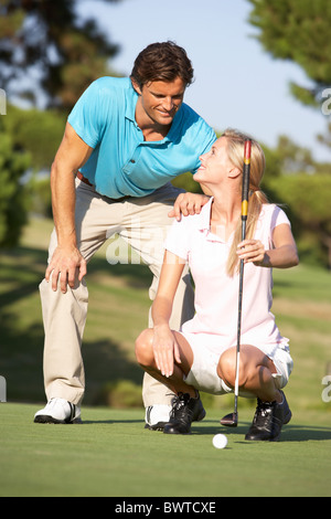 Woman playing golf lining up a putt on the green with her golf cart and ...