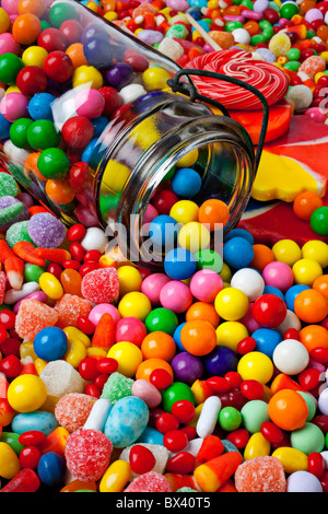 A still life of colorful candies spilling from a pink cup next to pink ...