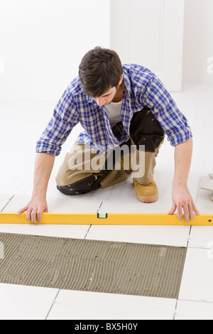 Home tile improvement - handyman with level laying down tile floor ...