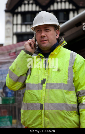 A man dressed in 'hi-viz' jacket and hard hat, makes a call on his ...