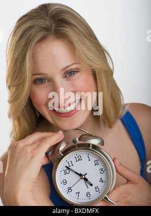 Happy young woman with alarm clock sitting in bedroom Stock Photo - Alamy