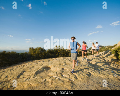 Man and woman trail runners rock-hopping in a river with fall foliage ...