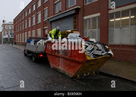 Scrap metal collectors searching through old office equipment in a skip ...