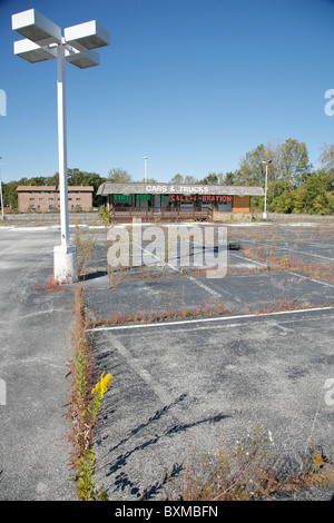 Empty abandoned car and truck dealer lot with weeds growing. Sign reads ...