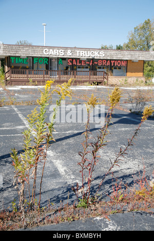 Empty abandoned car and truck dealer lot with weeds growing. Sign reads ...